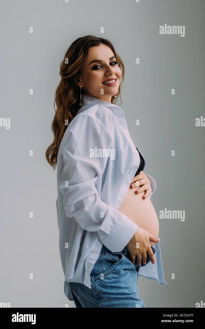 Side view of woman looking at pregnant belly posing against white ...