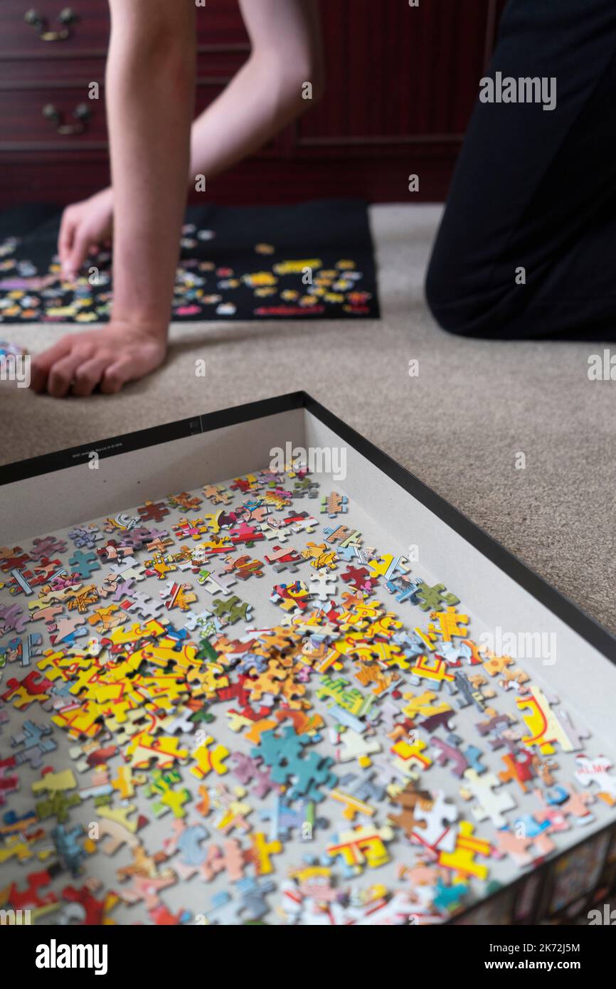 A teenage boy completing a jigsaw puzzle on a black cloth mat on the ...