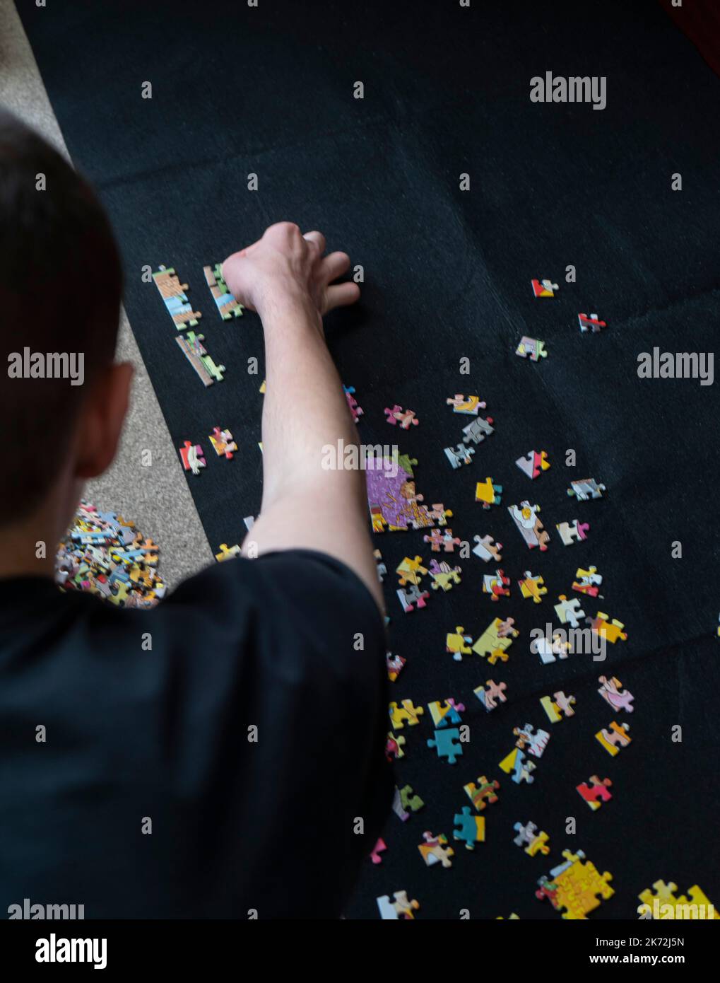 A teenage boy completing a jigsaw puzzle on a black cloth mat on the ...