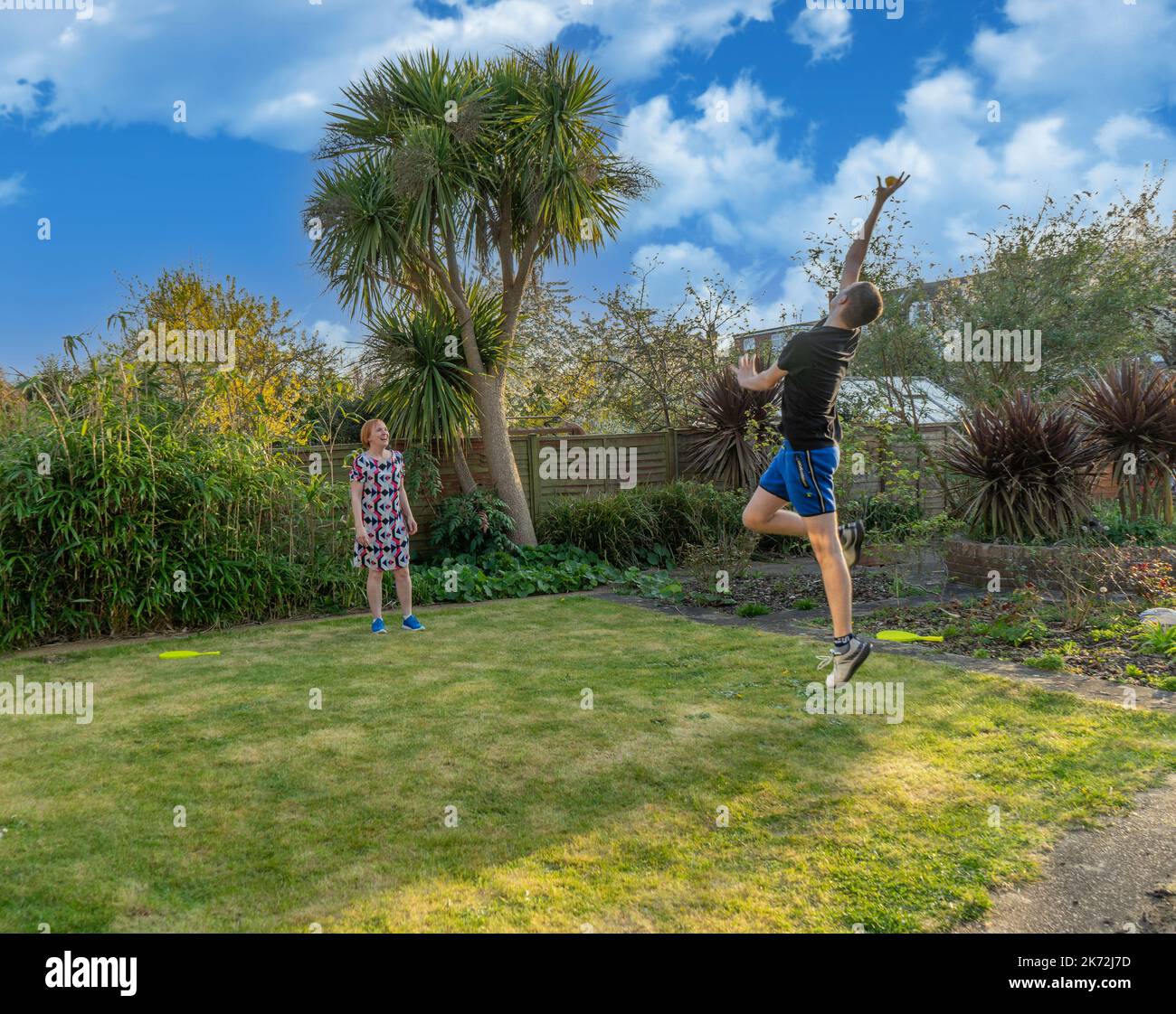 Teenage boy wearing sports gear jumping high to catch a tennis ball ...