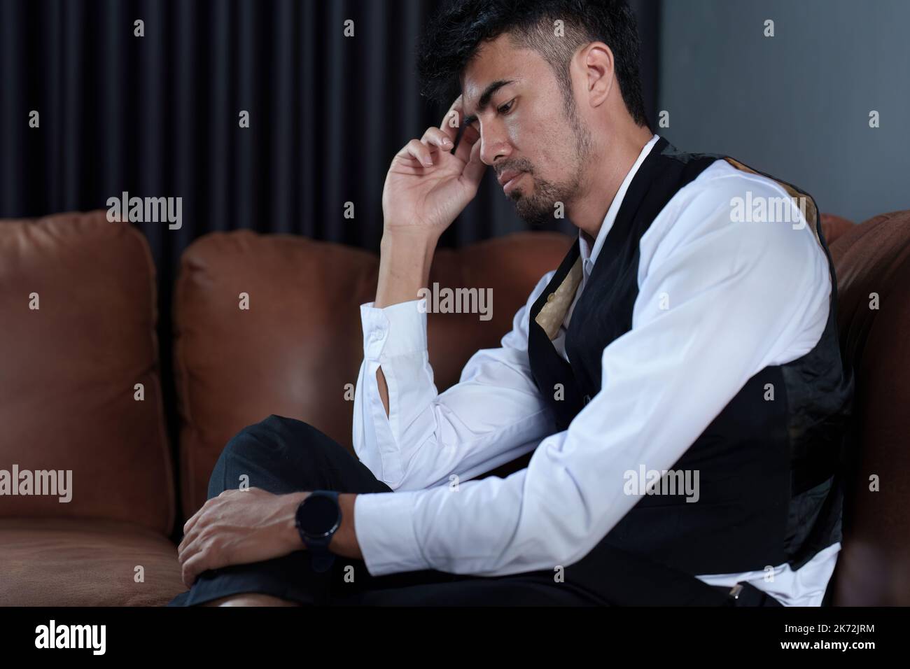 A portrait of a handsome Asian man sitting on the sofa with a ...