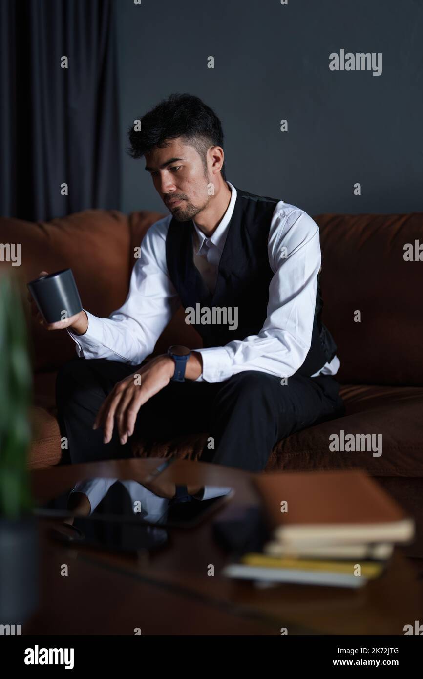 Portrait of a good looking and discreet Asian man sitting on the sofa ...