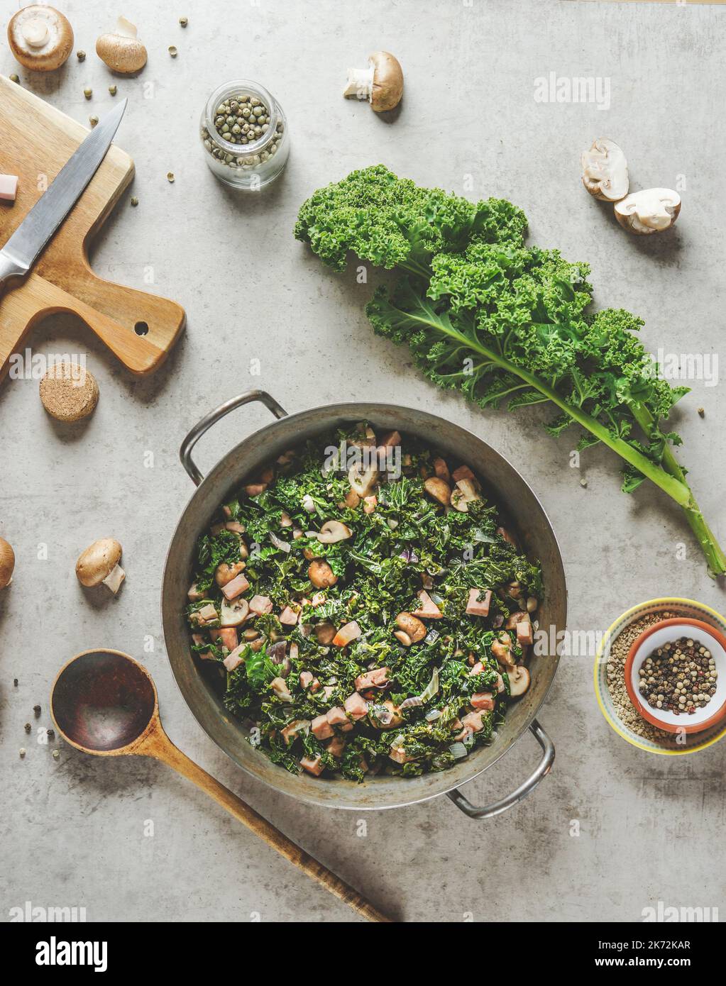 Cooking pot with stewed kale with mushrooms on kitchen table with spoon ...