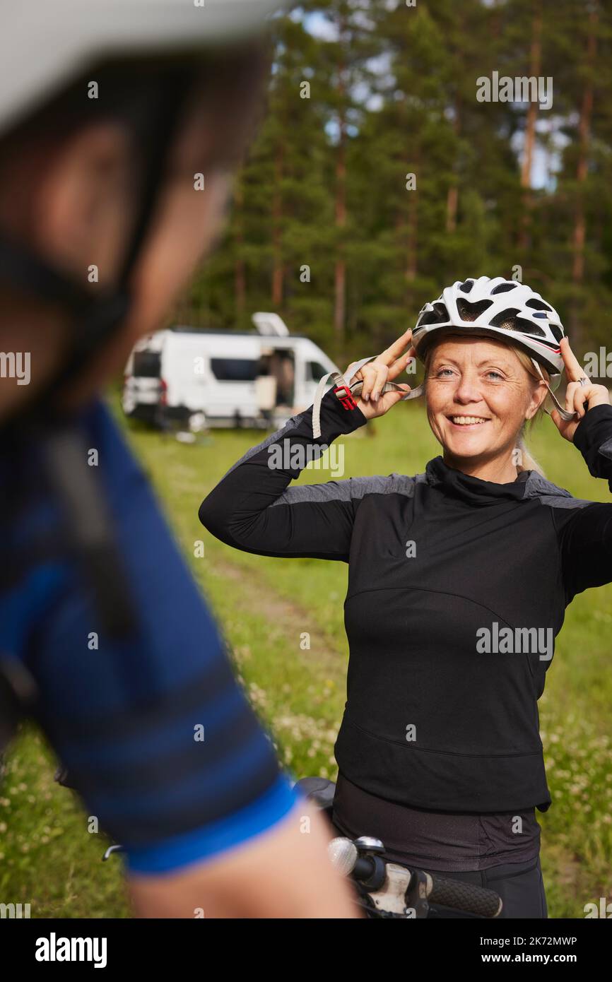 Smiling woman putting on bike helmet Stock Photo - Alamy