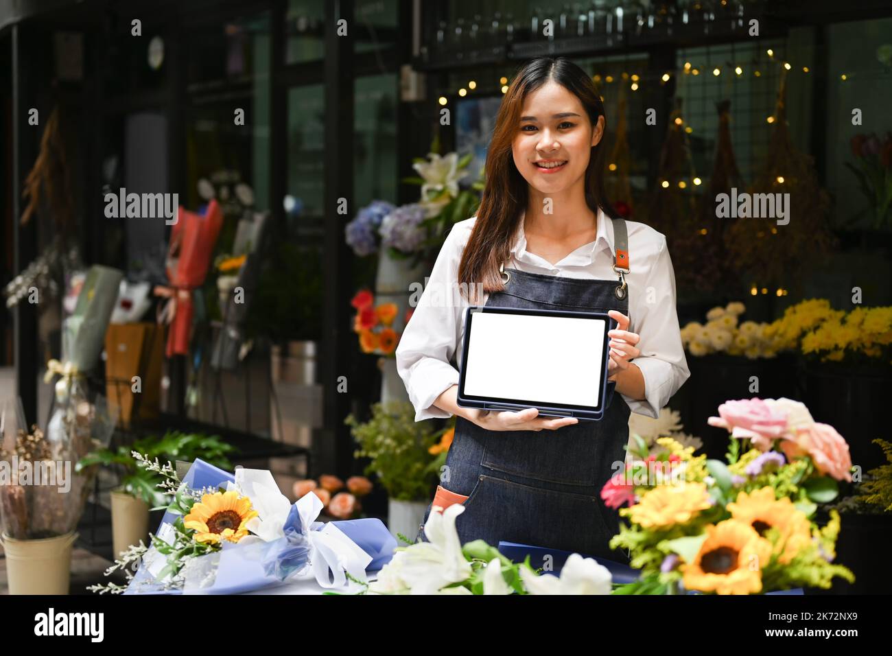 Smiling young female florist holding digital tablet standing front of ...
