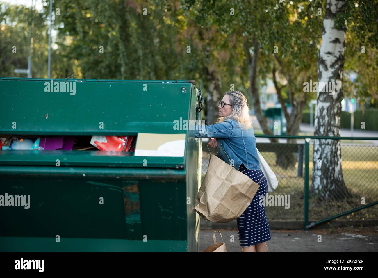 Blond woman throwing rubbish into waste bin Stock Photo - Alamy