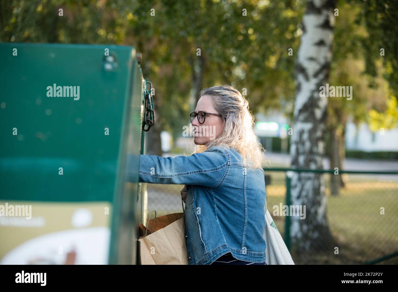 Blond woman throwing rubbish into waste bin Stock Photo - Alamy