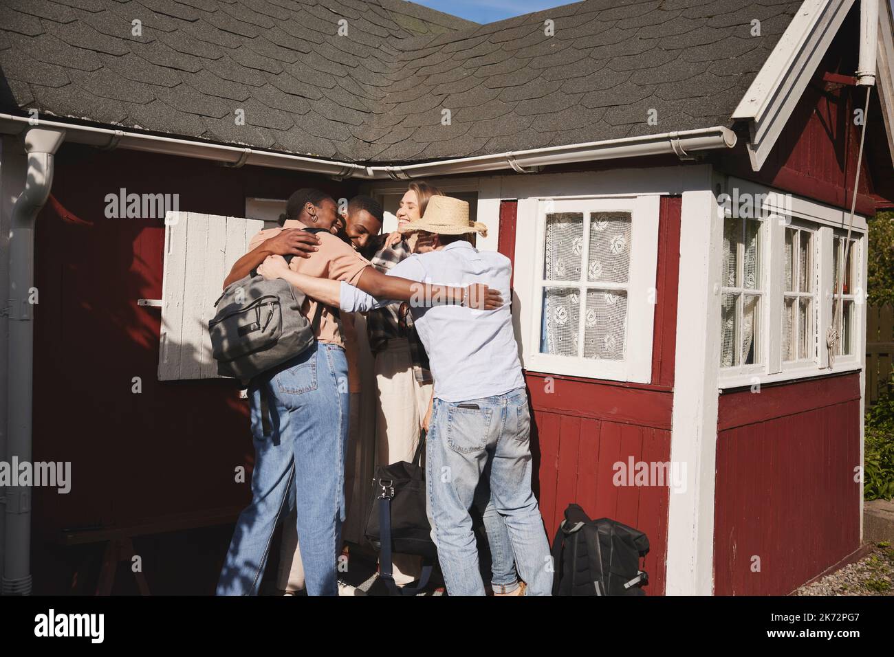 Smiling friends hugging in front of wooden house Stock Photo - Alamy