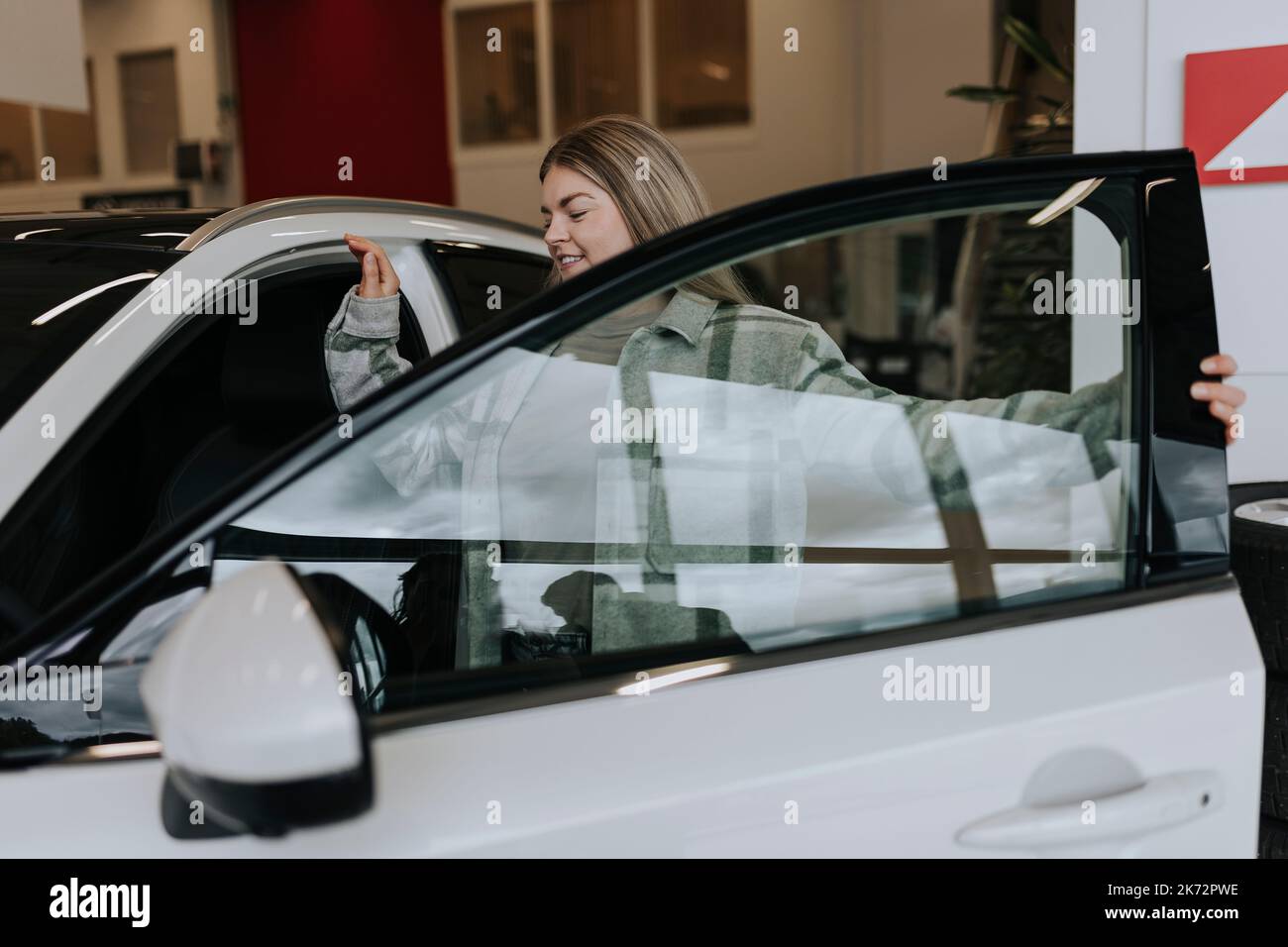 Young woman getting in car in car dealership Stock Photo - Alamy