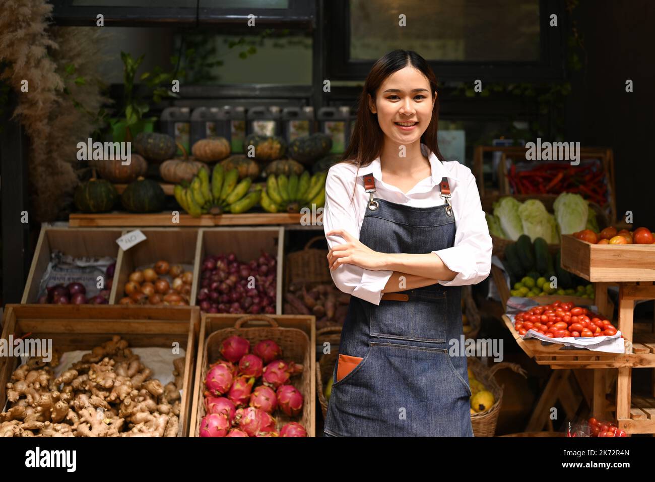 Portrait of friendly woman owner in apron standing with crossed arms ...