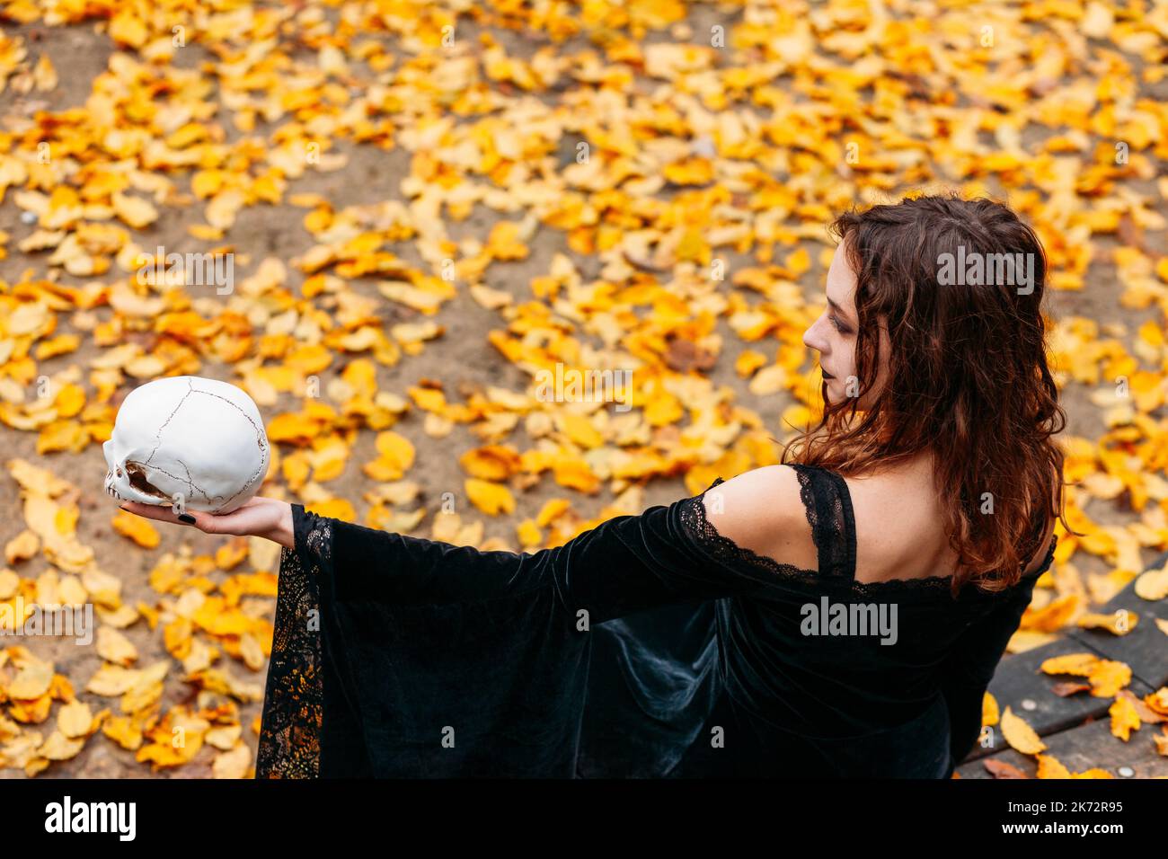 Brunette woman in black goth dress holding human skull in reaching hand ...