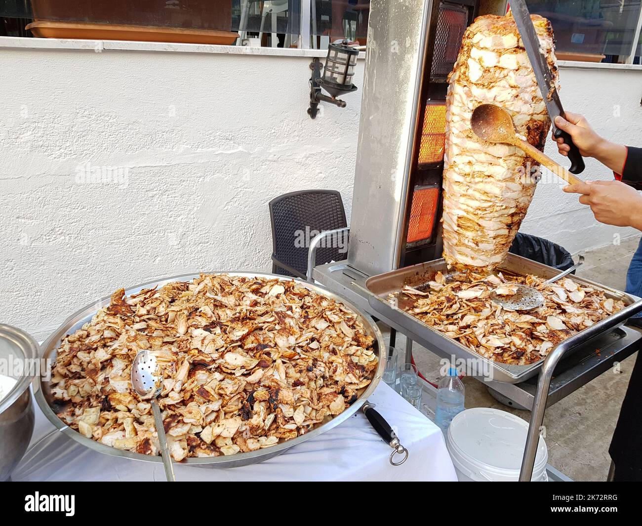 A cook cuts chicken meat on a skewer to cook shawarma. Traditional ...