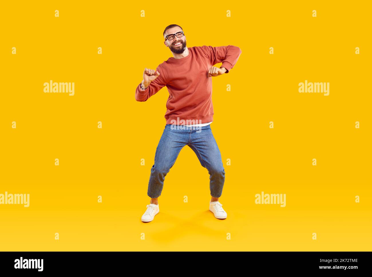 Happy funny young man in modern casual outfit dancing on yellow studio ...