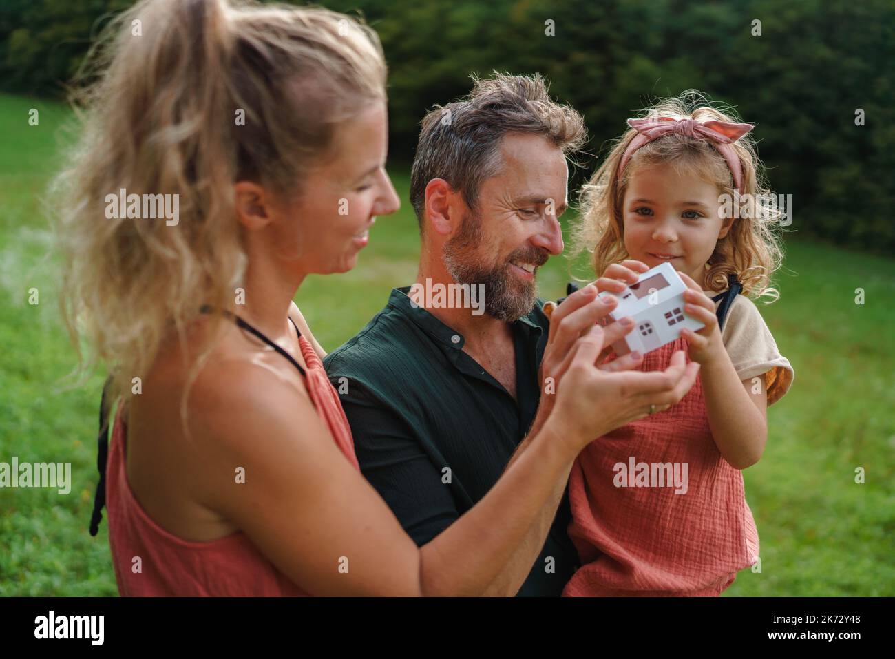 Little girl with her parents holding paper model of house with solar ...