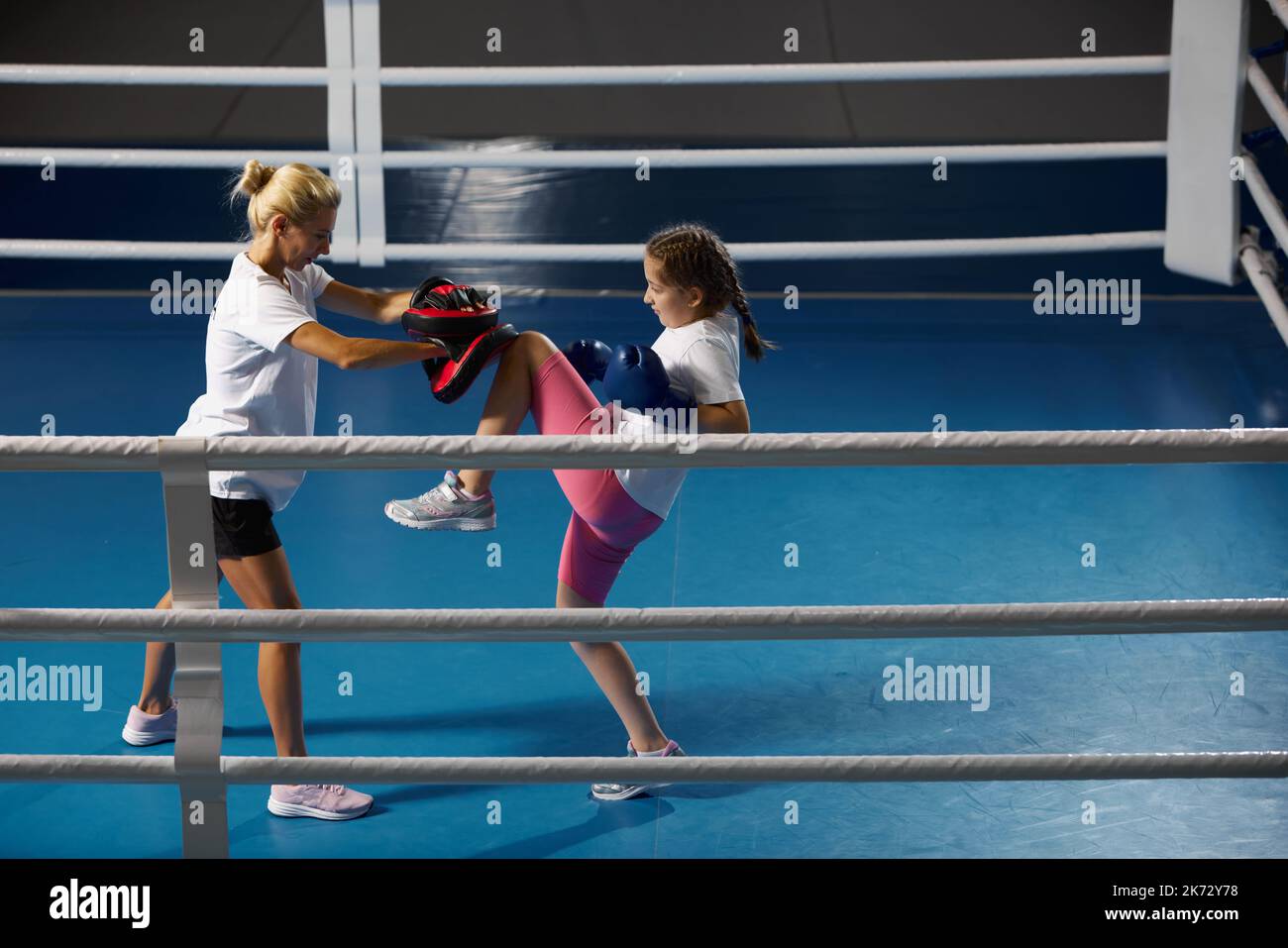 Knee kick. Two athletes, little girl, beginner kickboxer training with ...