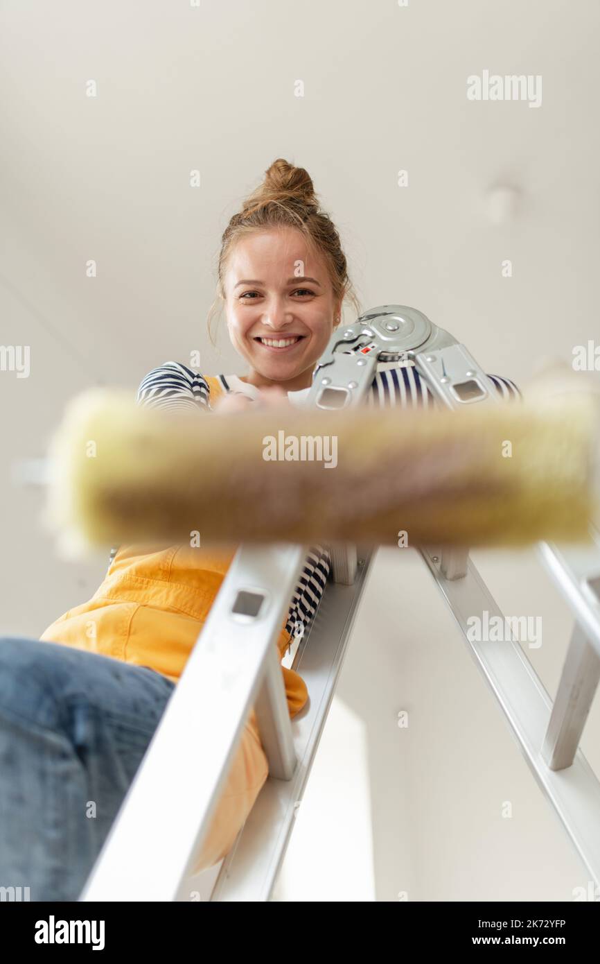 Low angle view of happy young woman remaking her new flat, painting ...