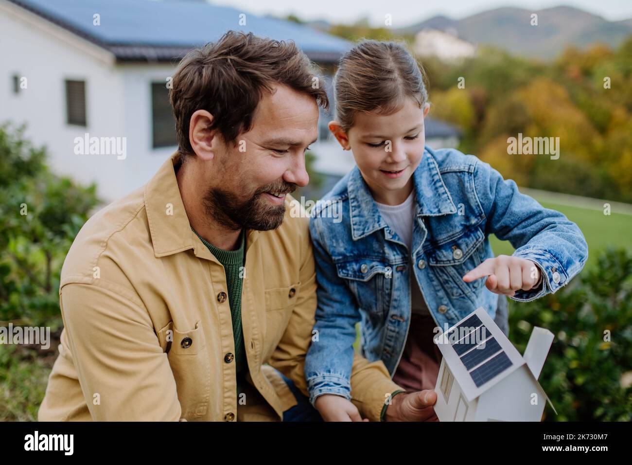 Little girl with her dad holding paper model of house with solar panels ...