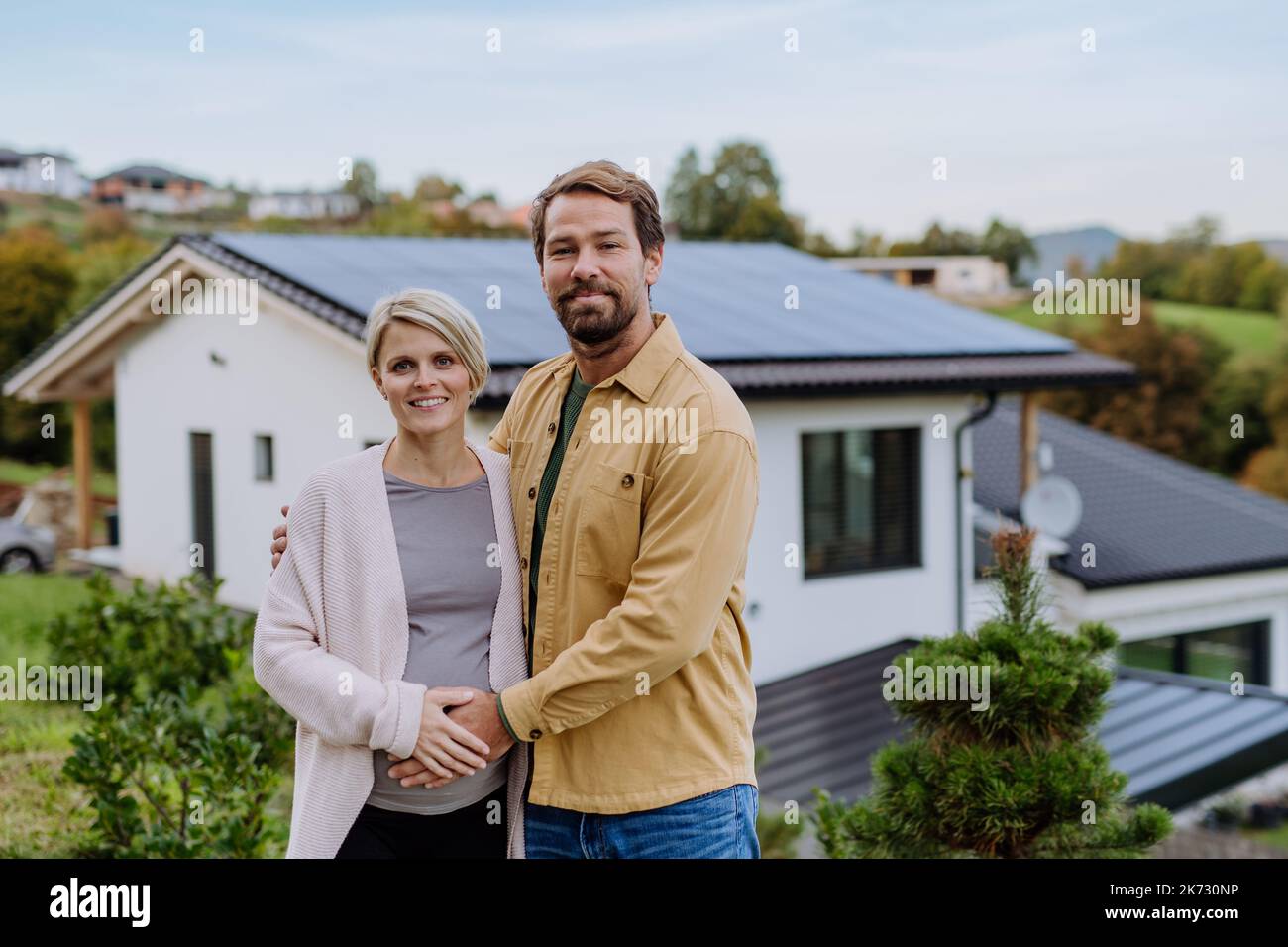 Happy man with his pregnant wife standing in front of their new house ...