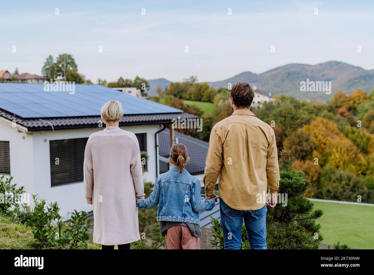 Rear view of family looking at their house with installed solar panels ...