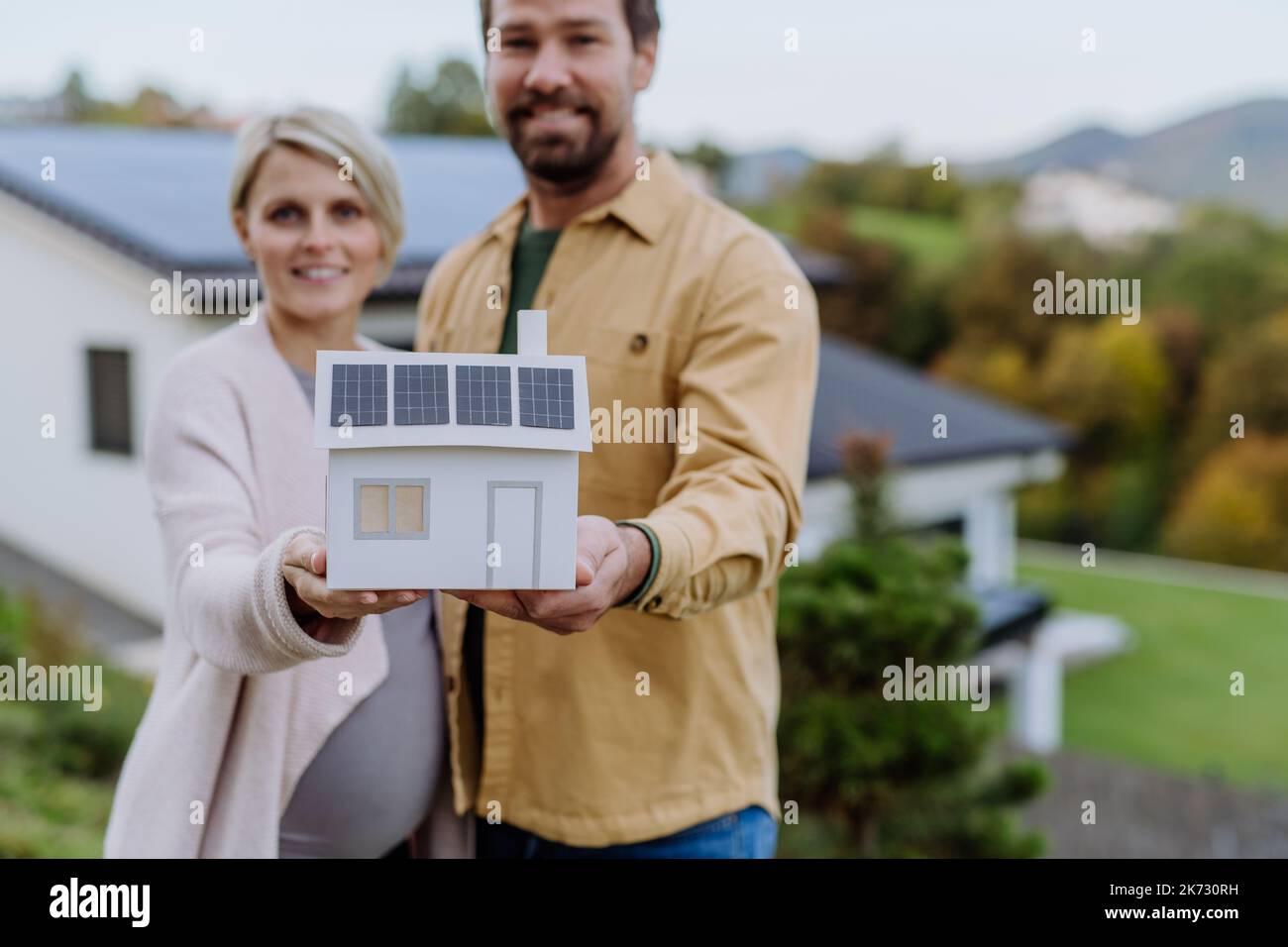 Close up of happy couple holding paper model of house with solar panels ...