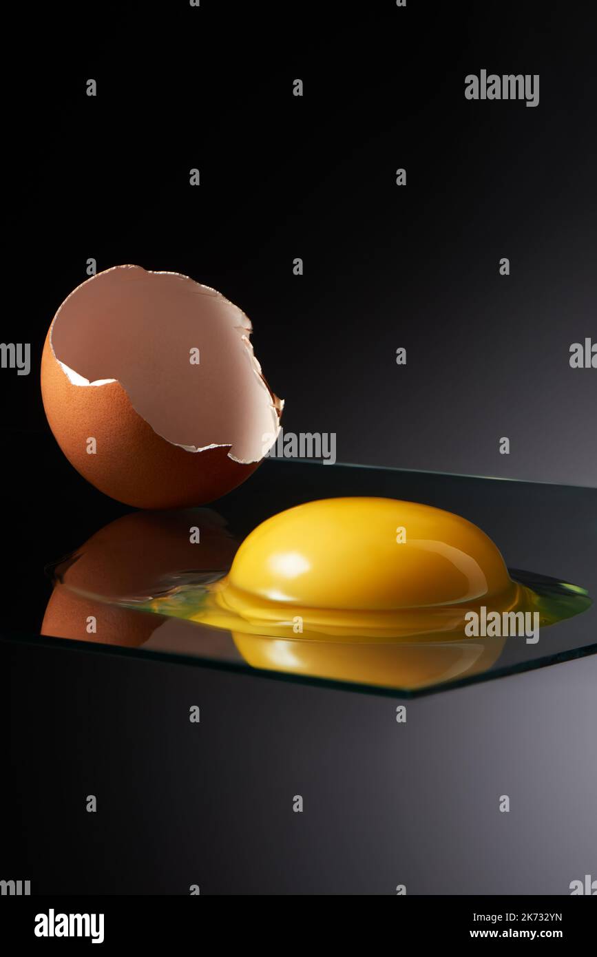 Vibrant yellow chicken egg yolk and half of broken shell on glass ...