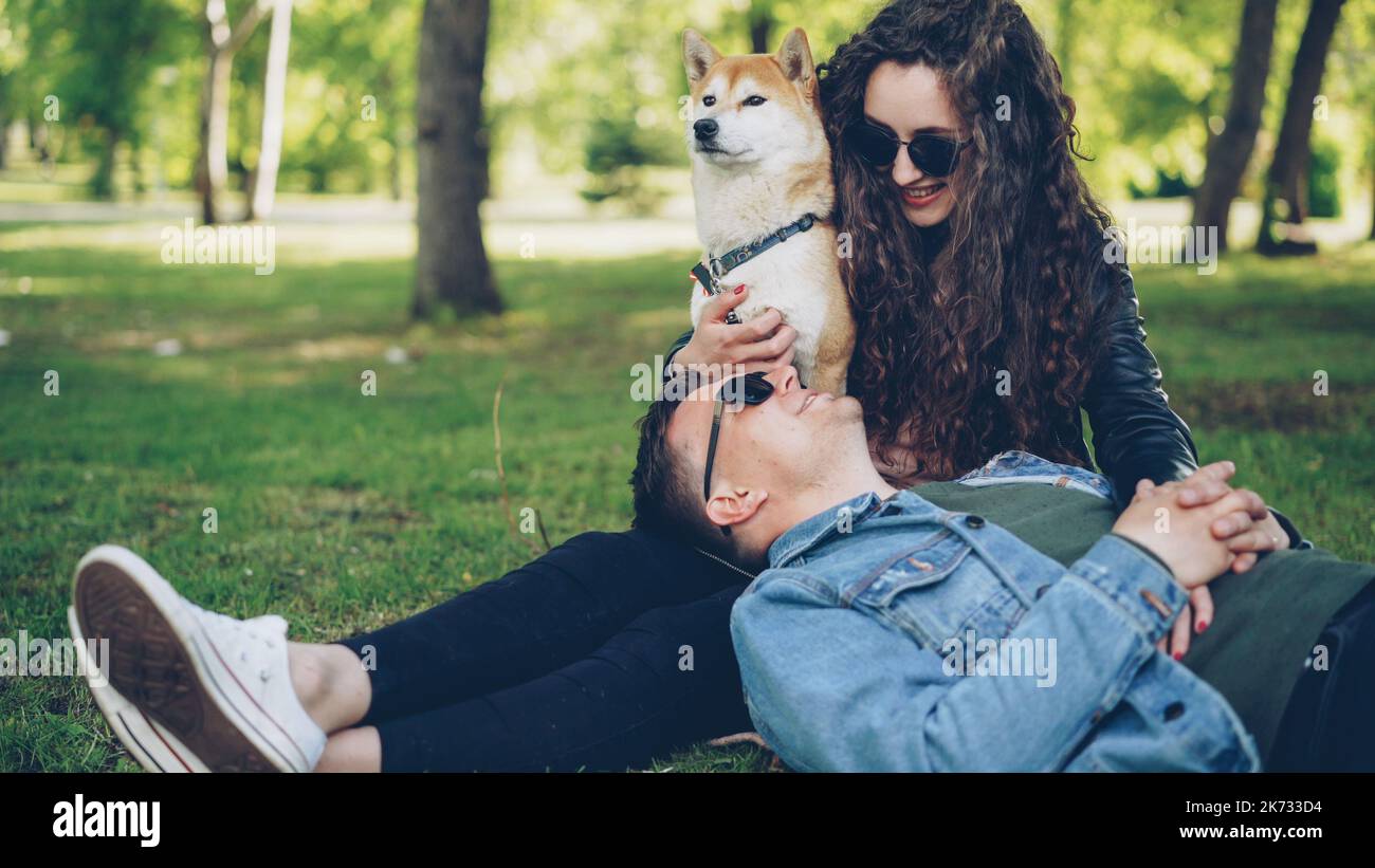 Cheerful young man is lying on the grass in the park with his head on ...