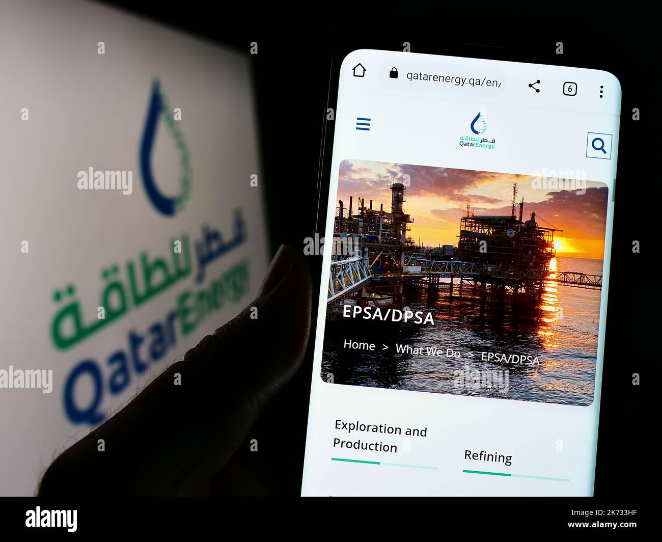 Person holding smartphone with webpage of Qatari petroleum company ...