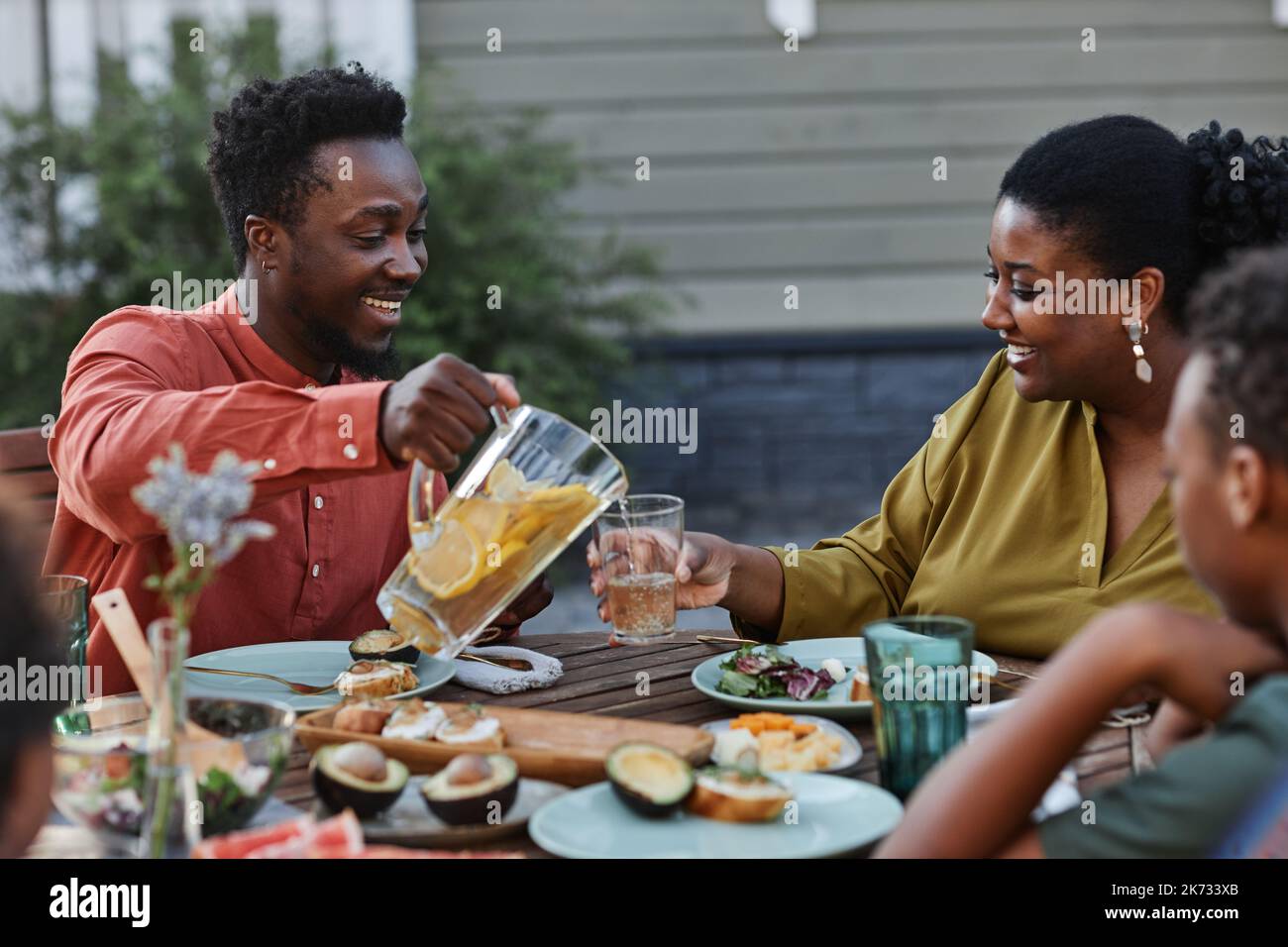 Portrait of smiling black man pouring lemonade to glass during family ...