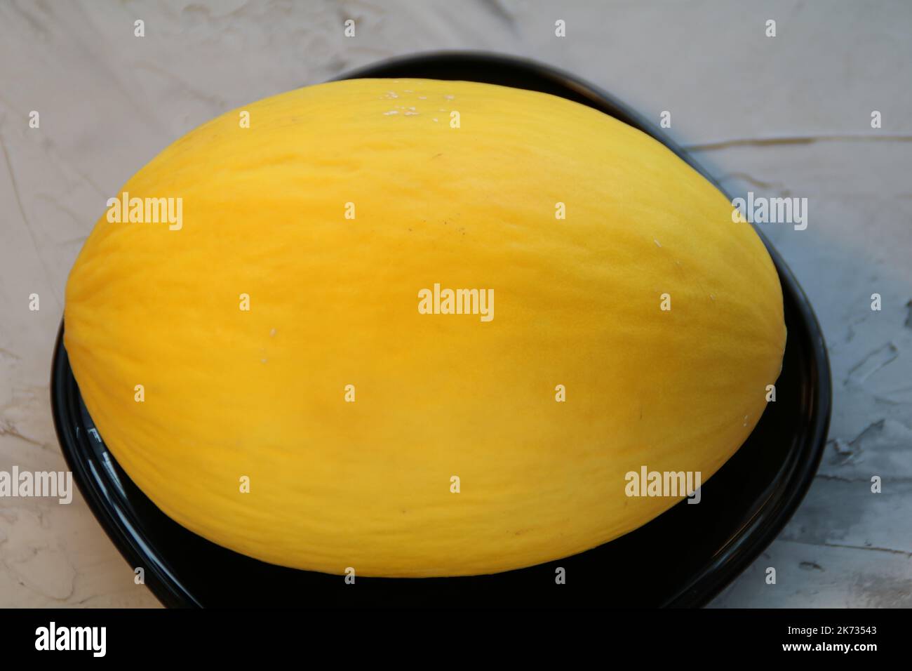 a yellow juicy melon lies on a black plate Stock Photo - Alamy