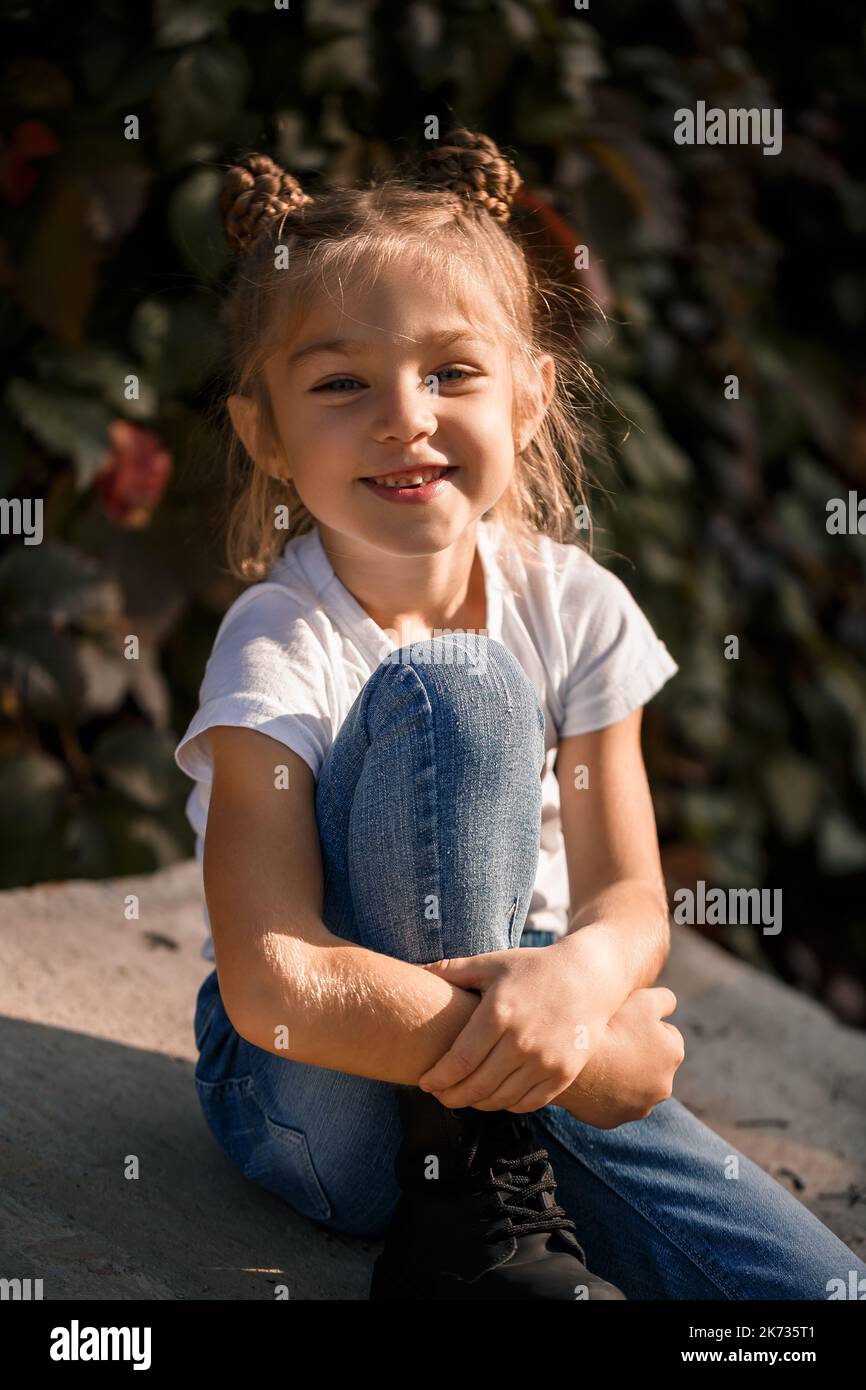 Street Photo Of A Little Beautiful Girl In Jeans And A White T Shirt On A Background Of Concrete