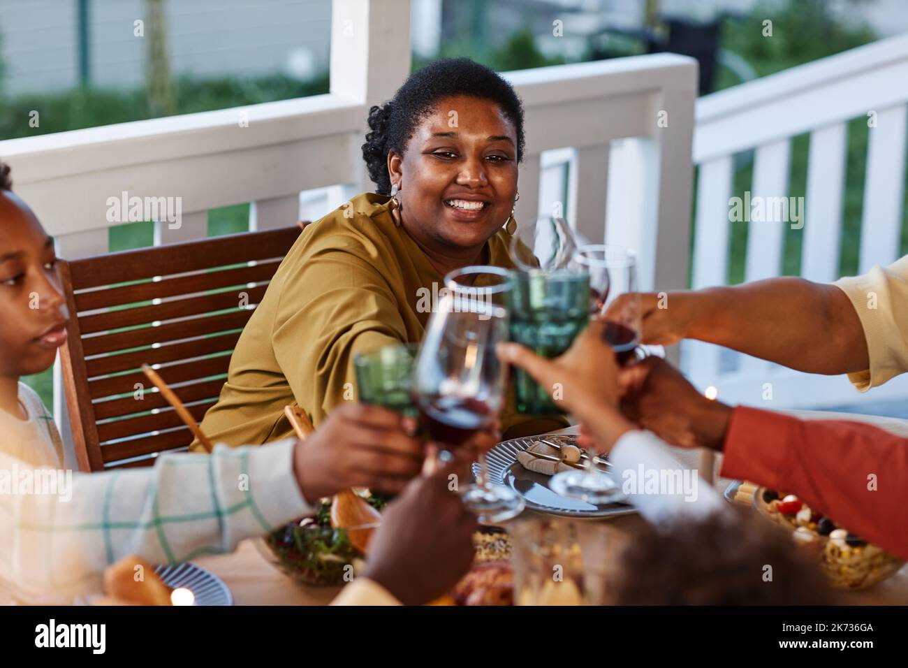 Portrait of smiling black woman clinking glasses over dinner table ...