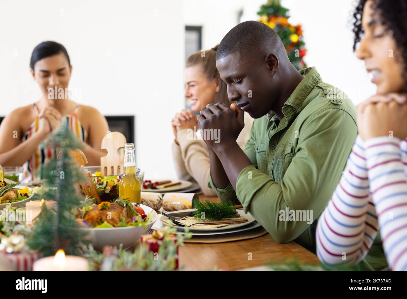 Happy diverse friends sitting at table and praying before dinner at ...
