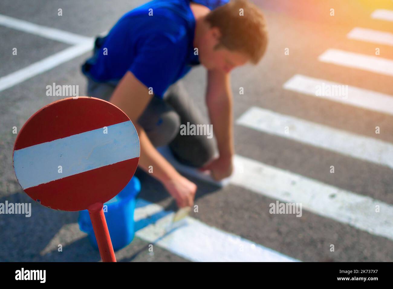 Road service worker paints striped pedestrian crossing on asphalt with ...