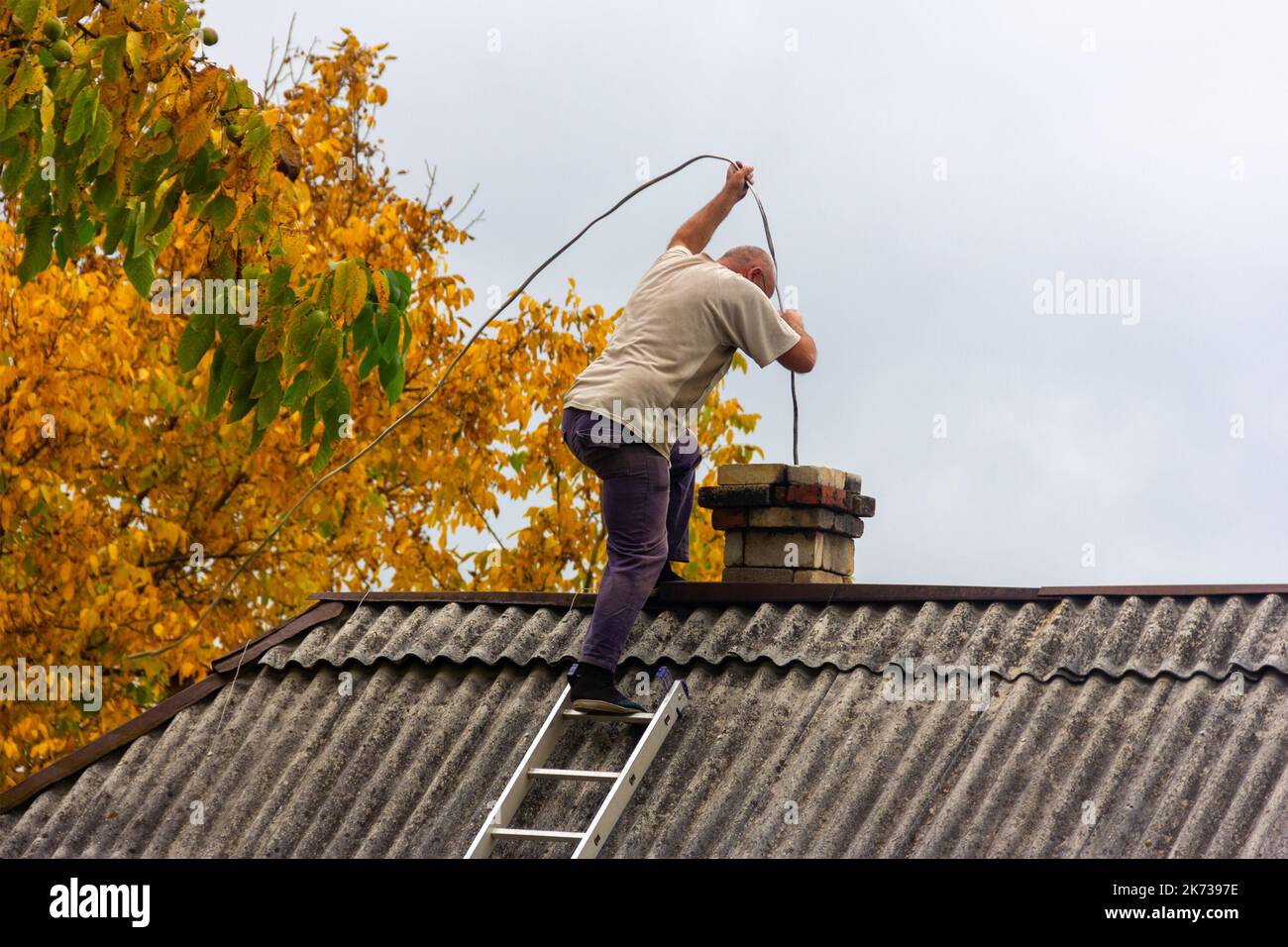 a male chimney sweep cleans the chimney from soot on the roof of a ...