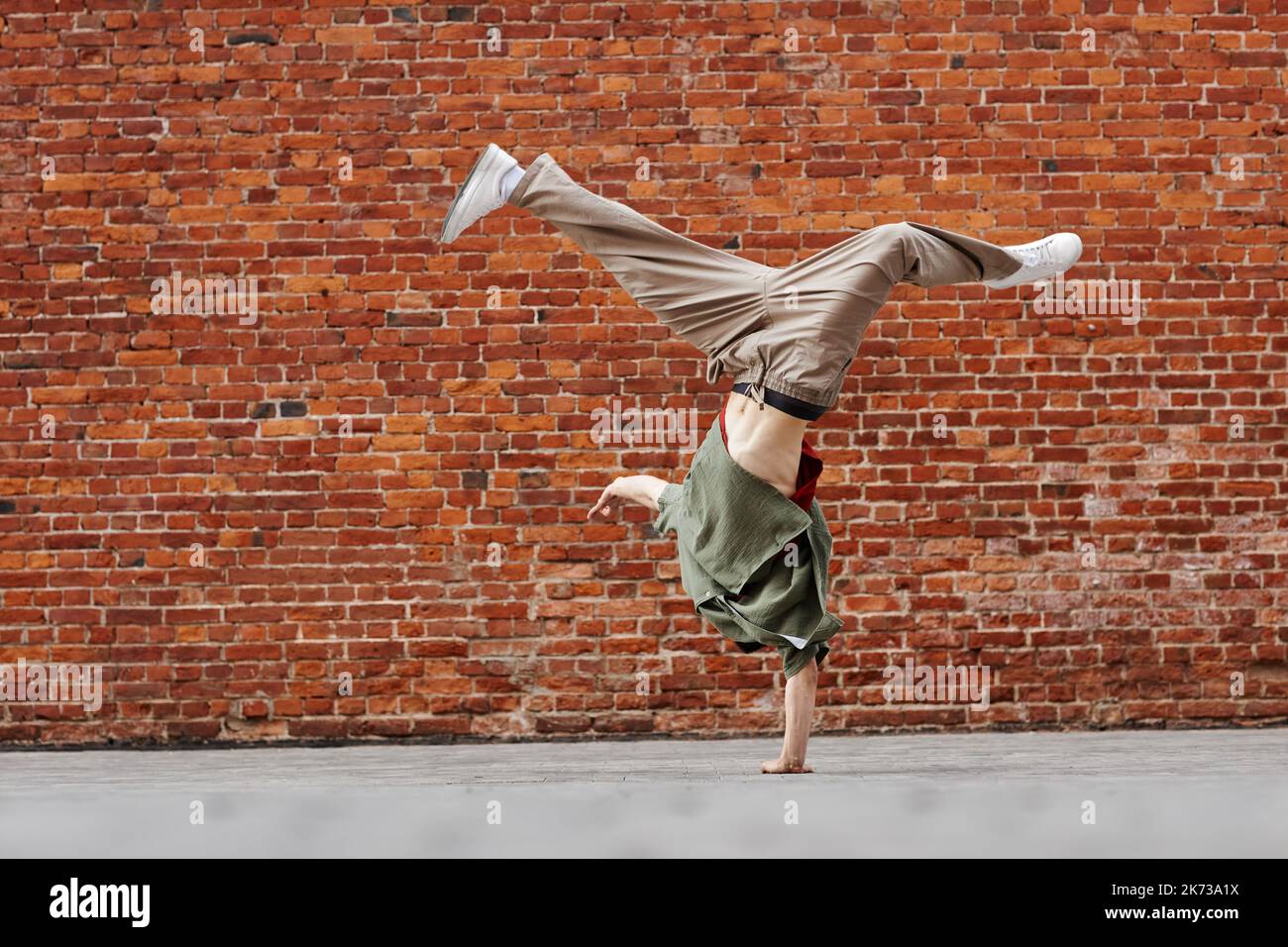 Motion shot of young man doing breakdance handstand pose against brick ...