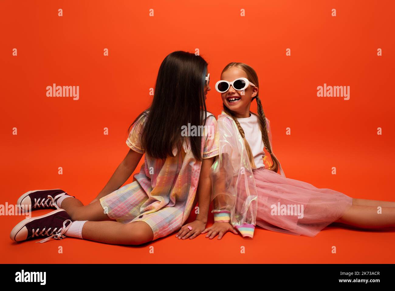 stylish preteen kids in sunglasses smiling at each other while sitting ...