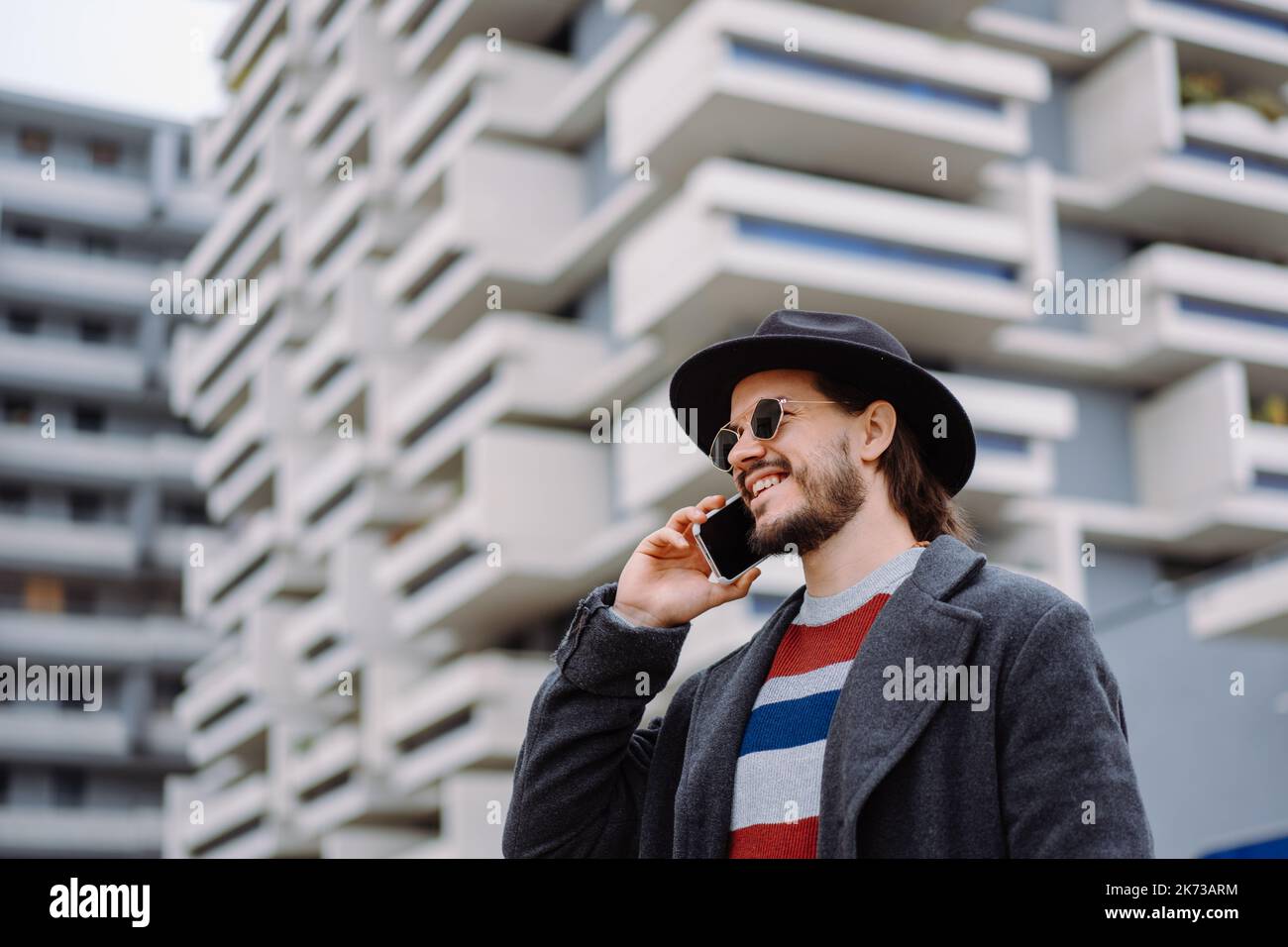 Young man in hat and sunglasses using smartphone while walking to work ...