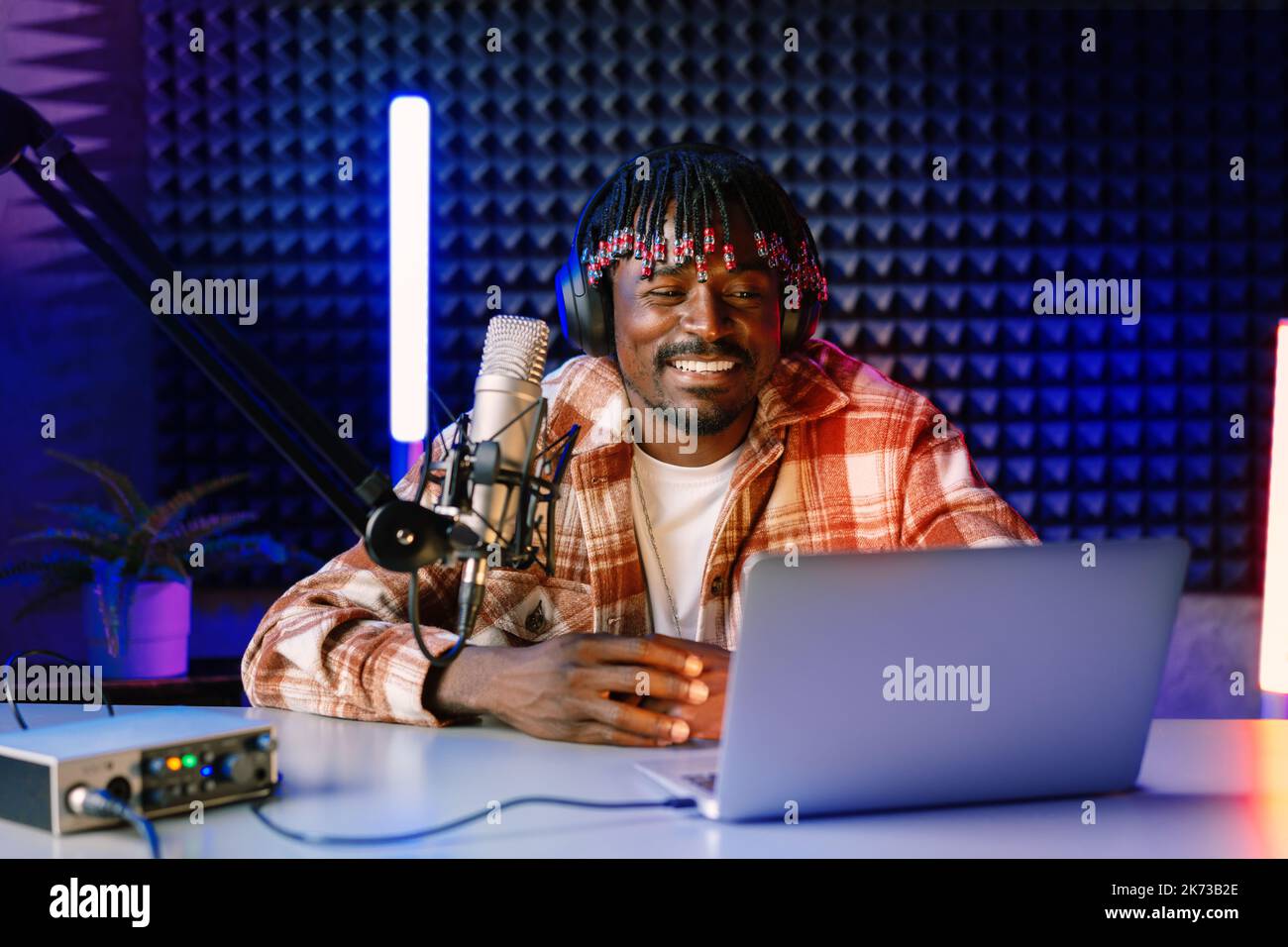 African radio host sitting at desk recording in studio with microphone ...