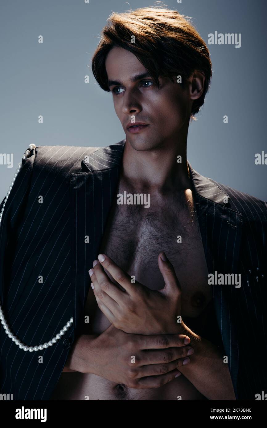 stylish man in trendy suit with pearl chain looking away on dark gray ...