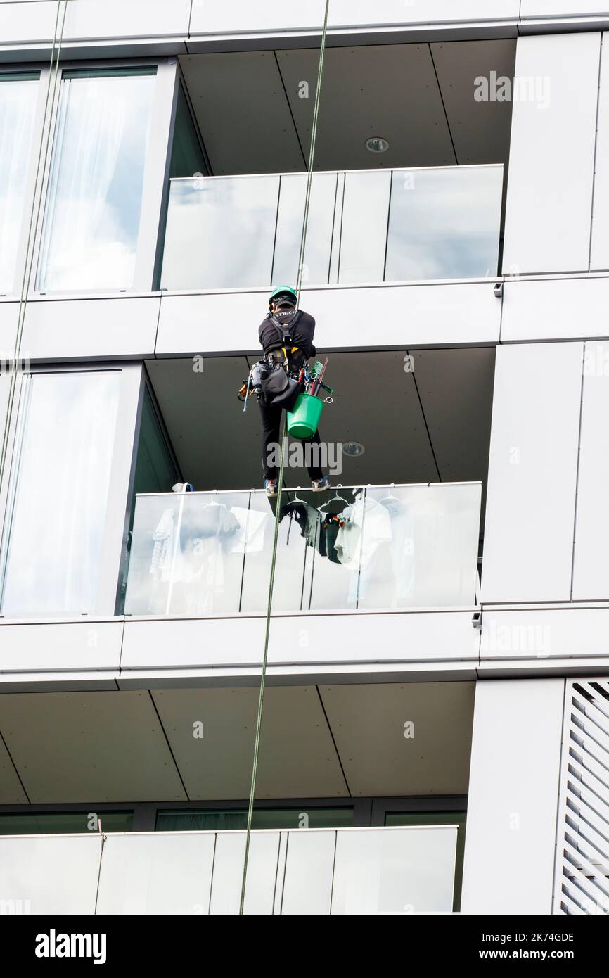 A man suspended on ropes cleaning the windows of an apartment block ...