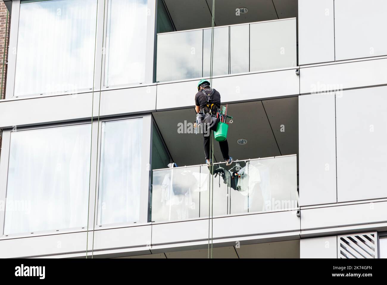 A man suspended on ropes cleaning the windows of an apartment block ...
