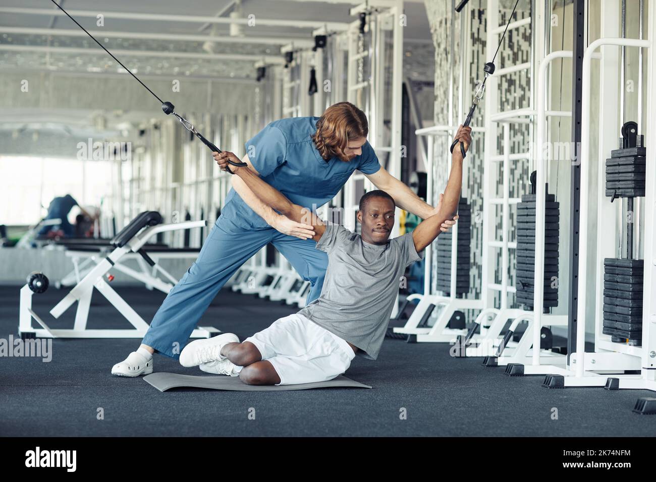 Young doctor in uniform helping patient with stretching exercises ...