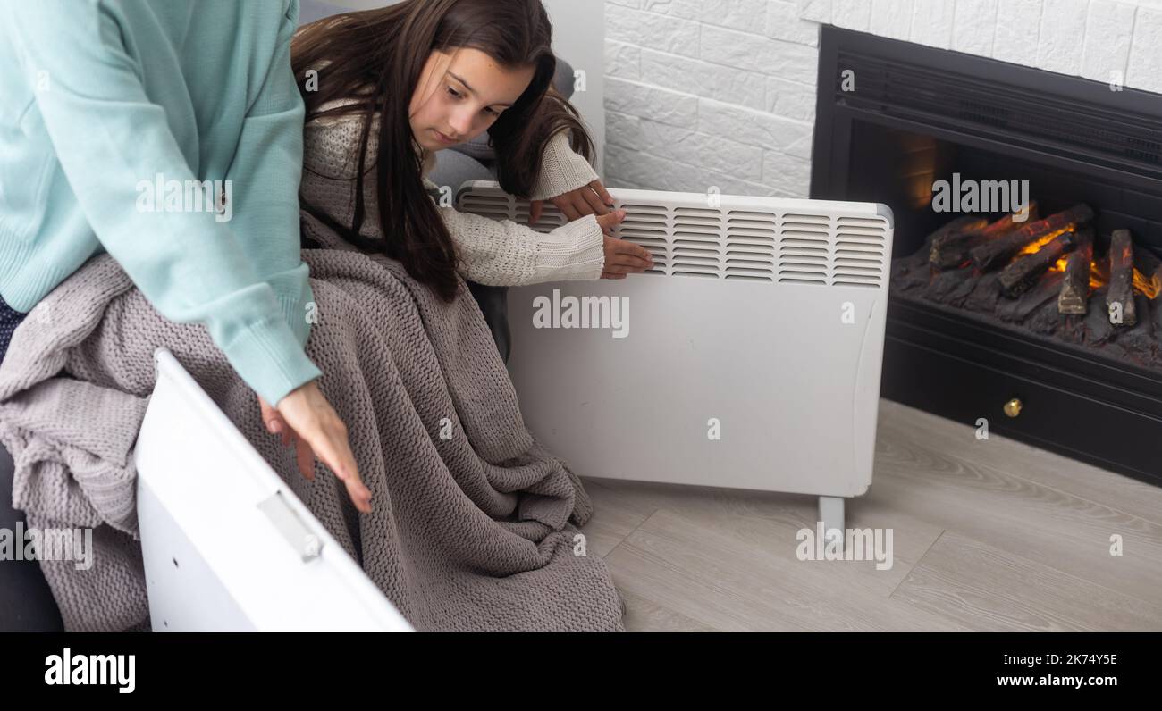 At the electric heater, people are warming themselves, covered with a ...