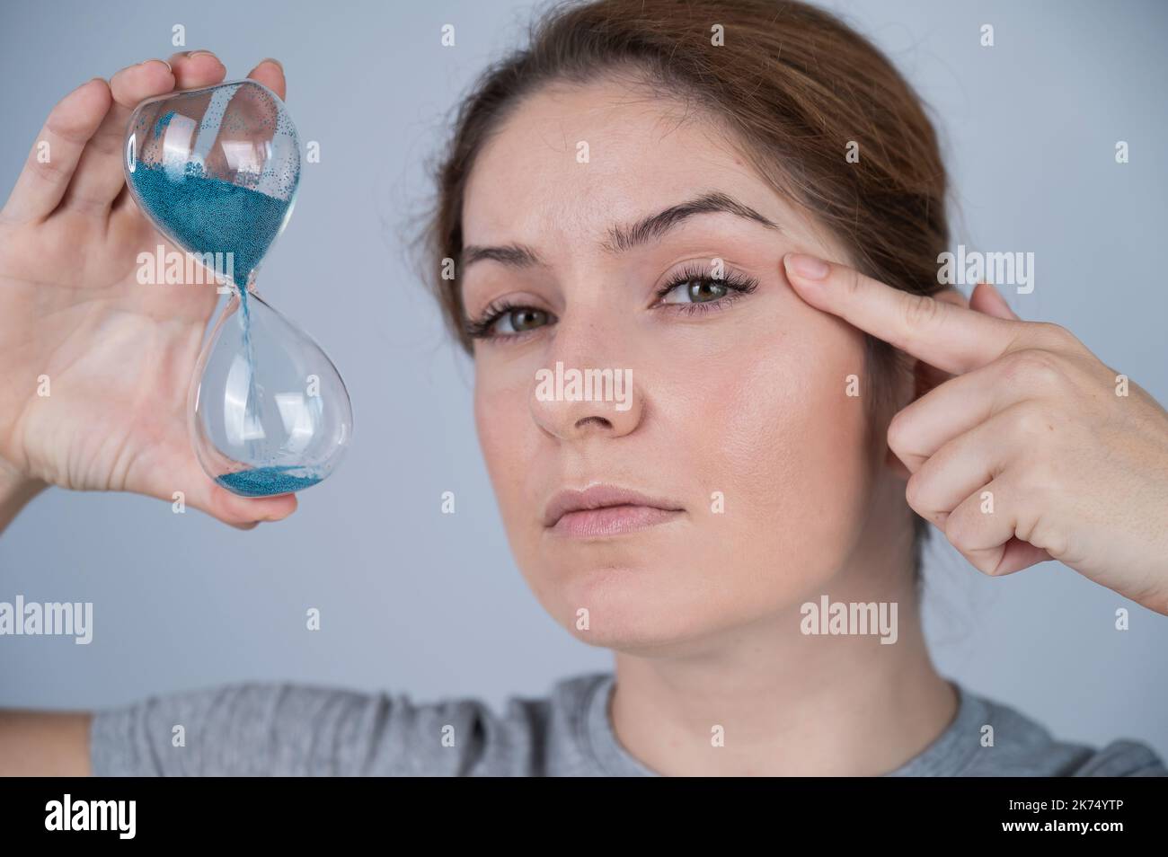 Caucasian red-haired woman holds an hourglass and examines the wrinkles ...
