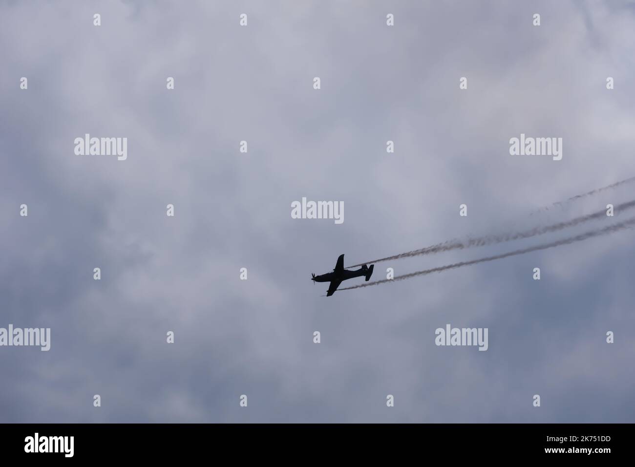 Small plane flying at a cloudy weather with smoke at back for an ...