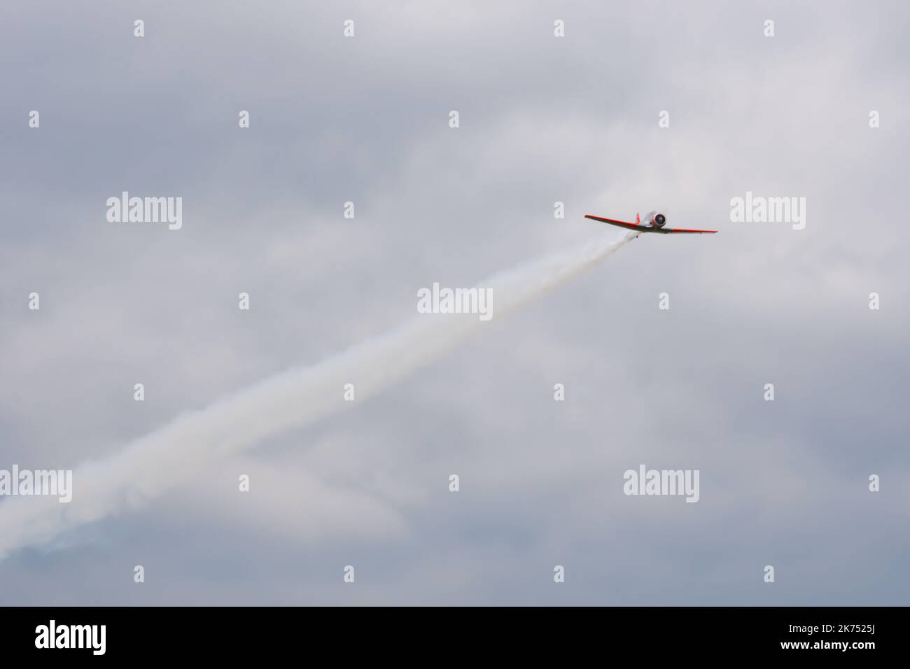 Small plane flying at a cloudy weather with smoke at back for an ...