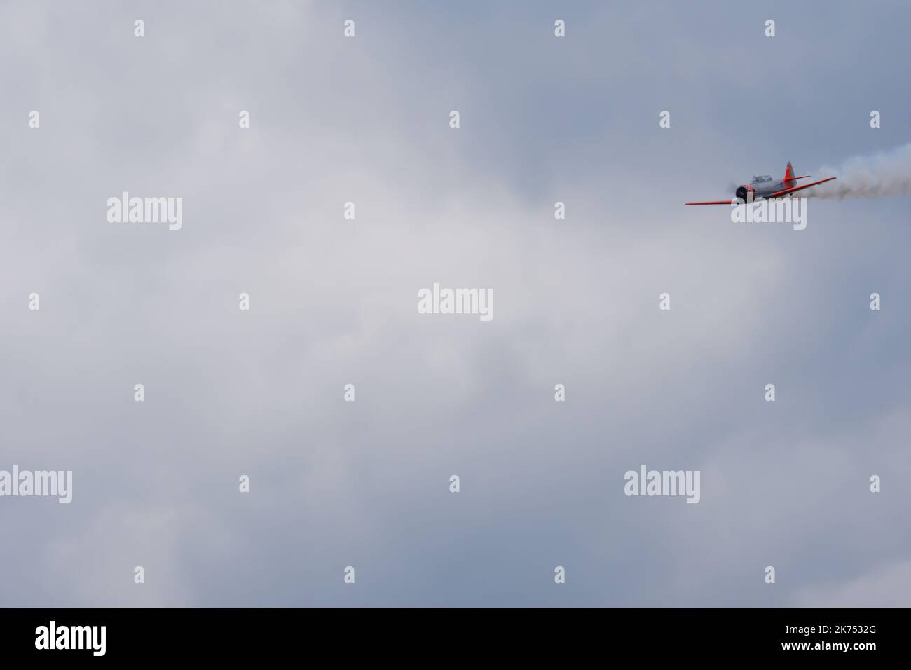 Small plane flying at a cloudy weather with smoke at back for an ...