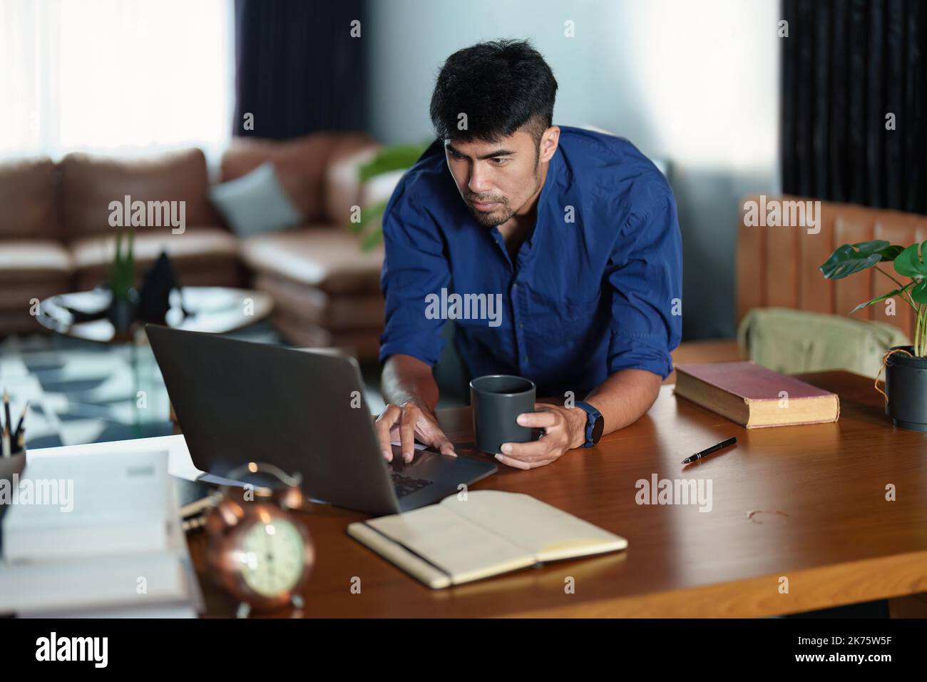 Portrait of an Asian man working on a computer and drinking coffee ...