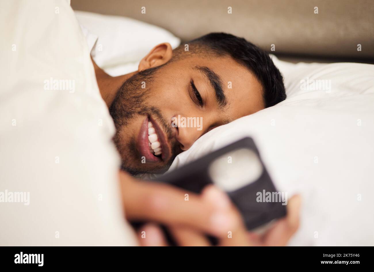 Sweet morning texts. a young man using his phone in bed at home Stock ...