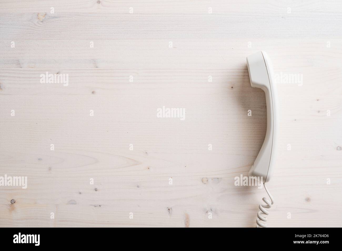 Simple white landline telephone handset placed on plain wooden ...